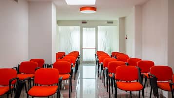 Uma sala de conferências com fileiras de cadeiras laranja, piso lustroso e uma luminária de teto brilhante.