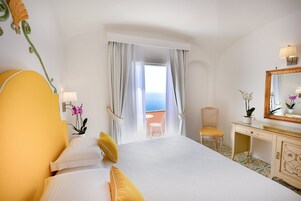 Quarto de hotel com cama, escrivaninha, cadeira e vista para o mar pela janela.