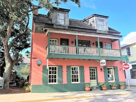 Um edifício de dois andares com varanda, persianas verdes e uma placa indicando 'Distrito Histórico da Cidade de Charleston'.
