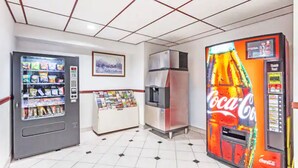 Uma área de distribuição automática com máquinas de lanches e bebidas, um frigorífico e uma máquina de Coca-Cola.