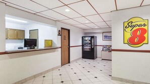 Um saguão de hotel com uma máquina de vendas automática, um balcão de recepção e um letreiro na parede com a inscrição "Super 8".