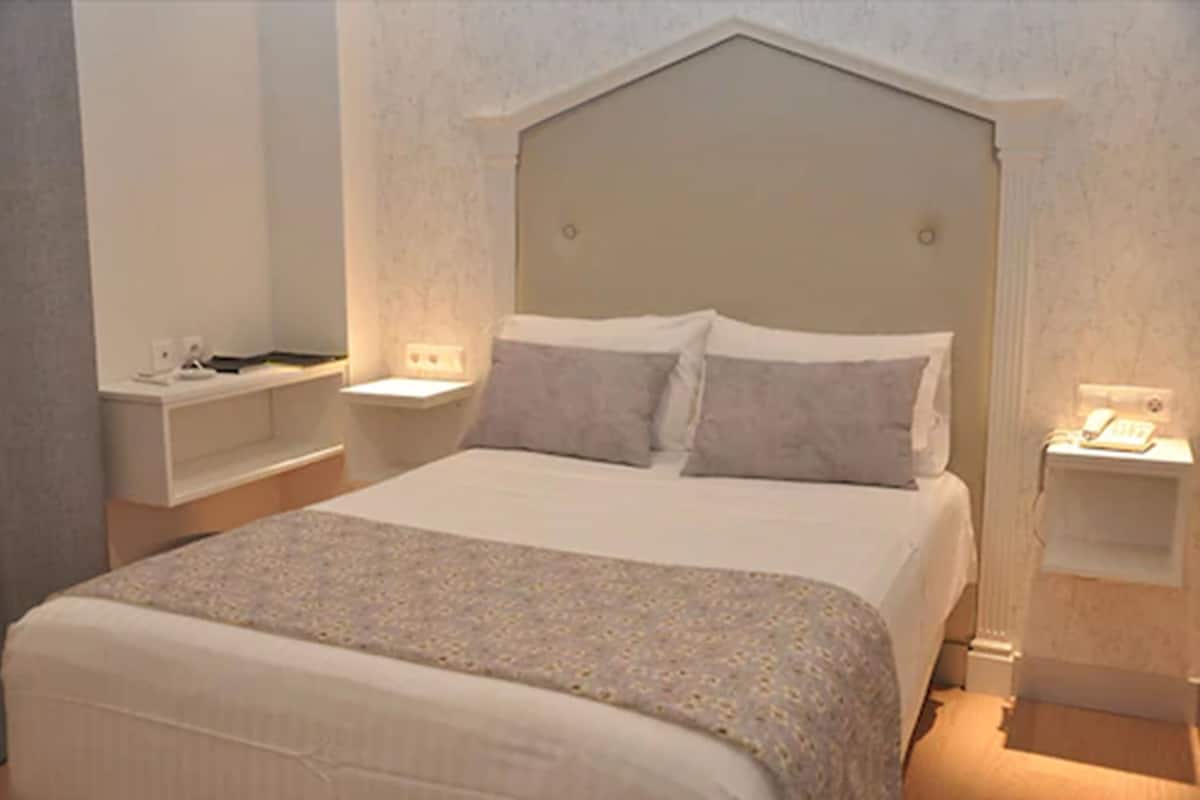 Cama bem arrumada com cabeceira, mesas de cabeceira e uma luminária em cada lado.