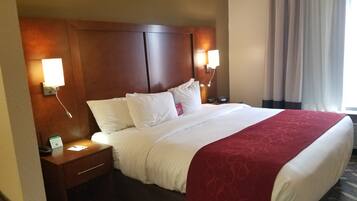 Quarto de hotel com uma cama grande, duas mesas de cabeceira, um painel de madeira na cabeceira e duas luminárias fixadas na parede.