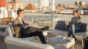 Terraço no telhado com cadeiras de lounge brancas, uma mesa e um vaso de planta.