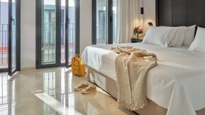 Quarto de hotel com uma cama grande, mesa de cabeceira, luminária e vista através de janelas em arco.