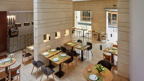 Uma área de refeições moderna com várias mesas e cadeiras, um bar com garrafas, e vista para uma piscina através de grandes janelas.