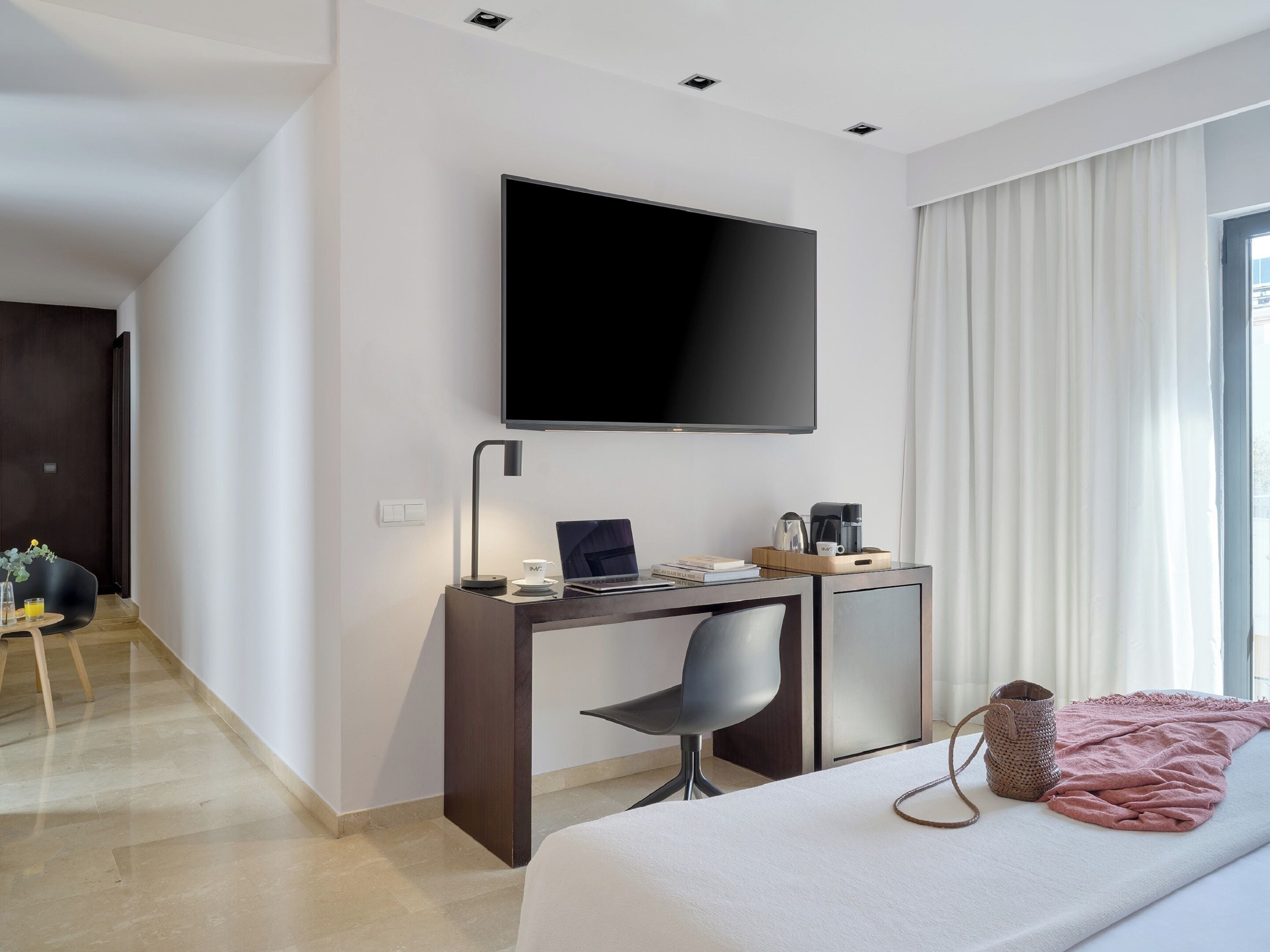 Quarto de hotel moderno com cama, escrivaninha com cadeira, televisão de tela plana e janela com cortinas.