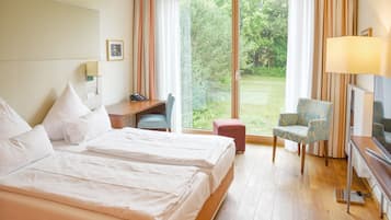 Quarto de hotel com duas camas, uma escrivaninha, uma cadeira, televisão e vista para o exterior.