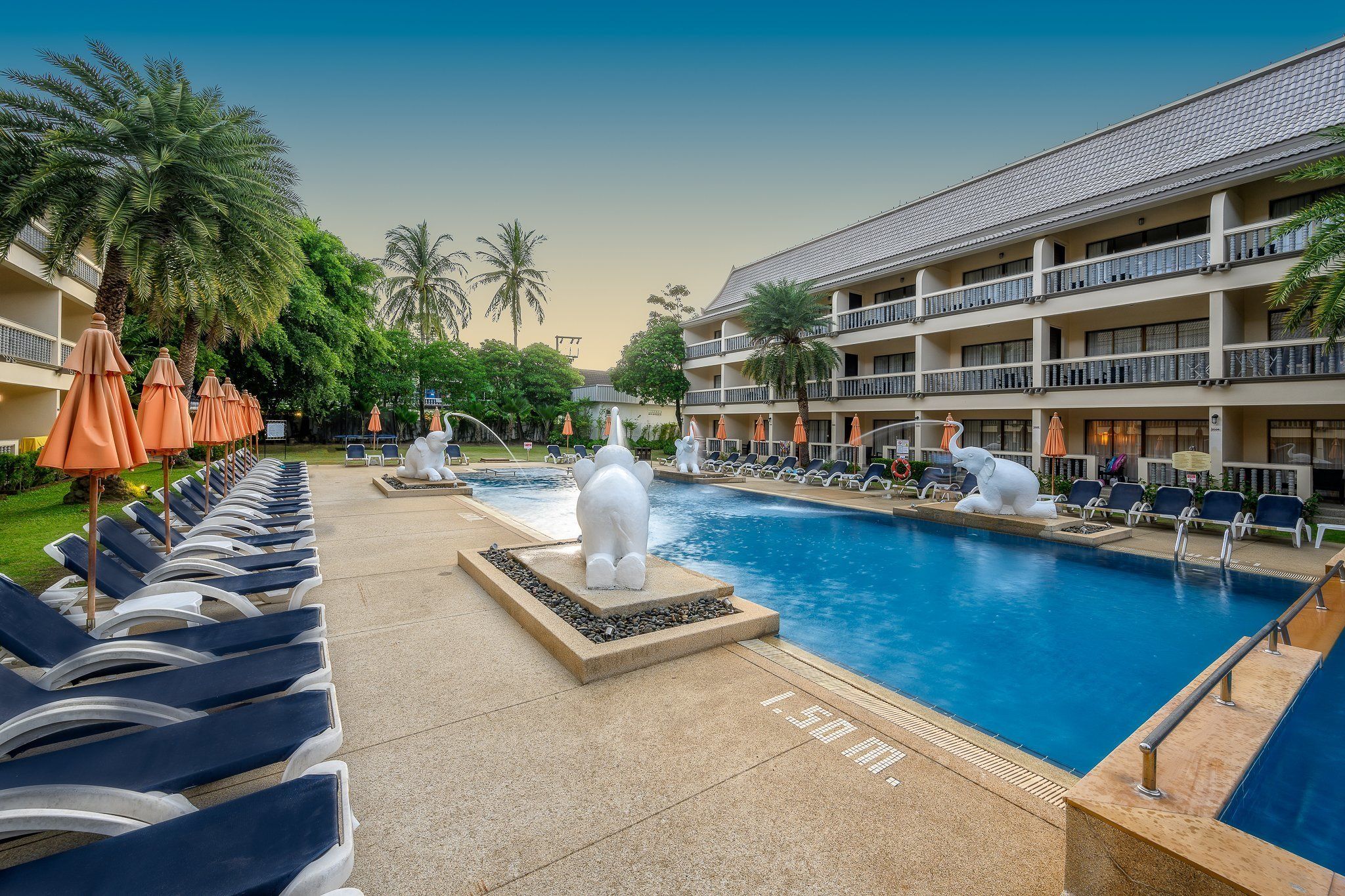 Uma área de piscina de hotel com espreguiçadeiras, guarda-sóis e uma estátua.