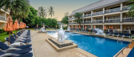 Uma área de piscina de hotel com espreguiçadeiras, guarda-sóis e uma estátua.