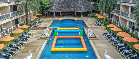 Área de piscina de hotel com vários níveis, piscina central com escorrega e espreguiçadeiras com guarda-sóis.