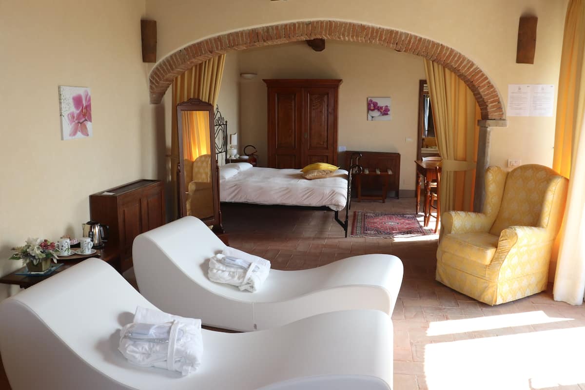 Quarto de hotel com cama, área de estar com cadeiras, armário de madeira e espelho.