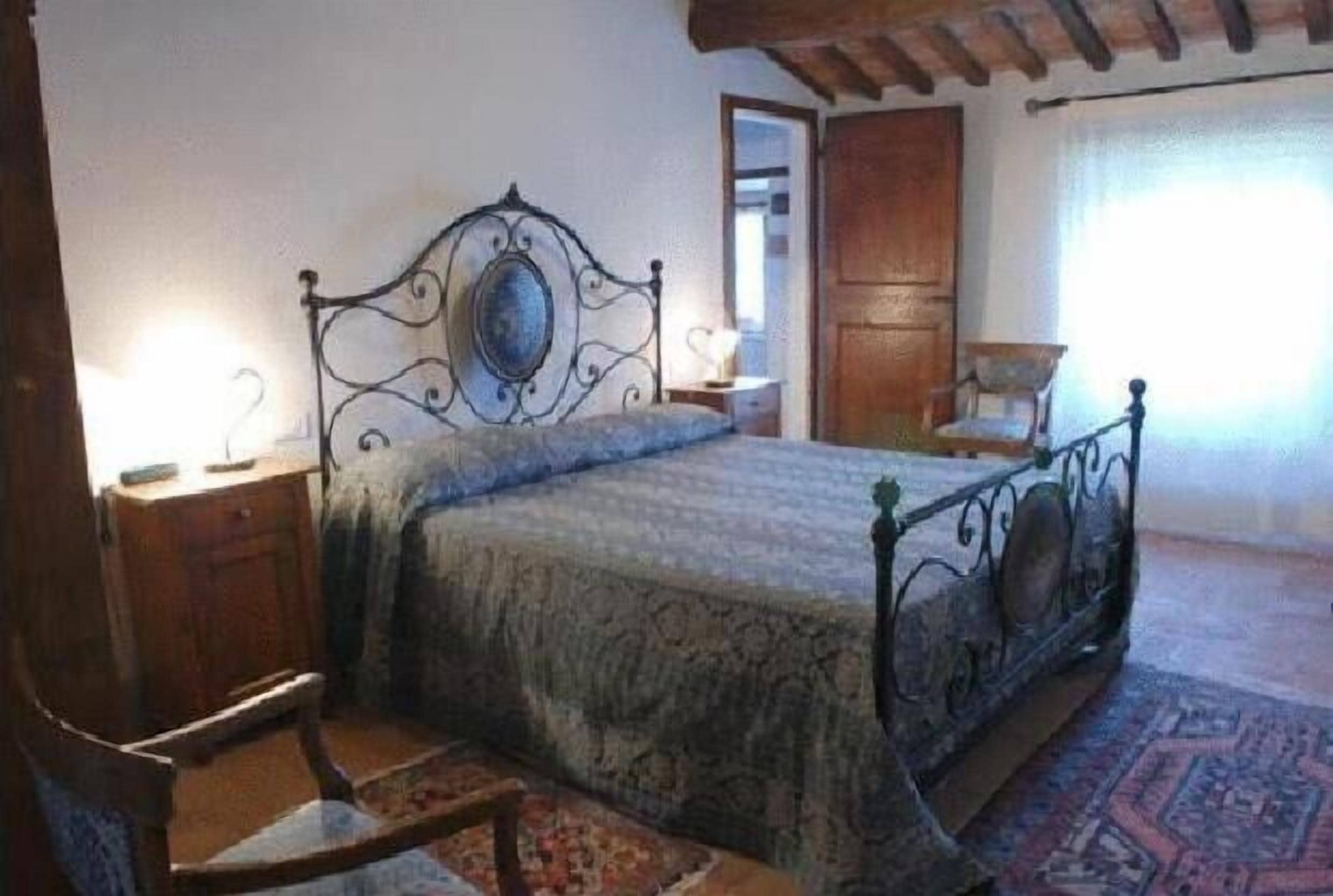 Quarto com estrutura de cama de metal, cabeceira de madeira e mesa de cabeceira com abajur.
