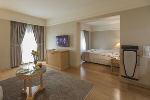 Quarto de hotel com cama, mesa de cabeceira, escrivaninha, cadeira, televisão e telefone.