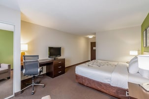 Quarto de hotel com cama, escrivaninha com televisão, uma cadeira e abajur.
