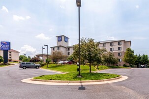 Um hotel Sleep Inn com um estacionamento, uma rotatória central e um edifício com várias janelas e uma torre.