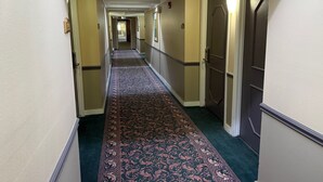 Um corredor de hotel com carpete estampado, portas em ambos os lados e teto com iluminação embutida.