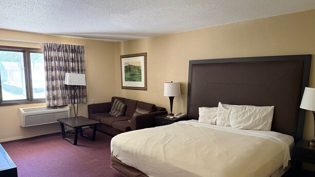 Quarto de hotel com uma cama grande, um sofá, uma escrivaninha e uma janela com cortinas.
