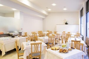 Uma área de refeições com mesas preparadas para o pequeno-almoço, incluindo croissants e fruta.