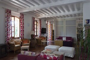 Uma sala de estar ampla, com lareira, móveis de vime e uma televisão.