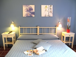 Quarto com uma cama, duas mesas de cabeceira, um criado-mudo, um abajur e duas pinturas na parede.