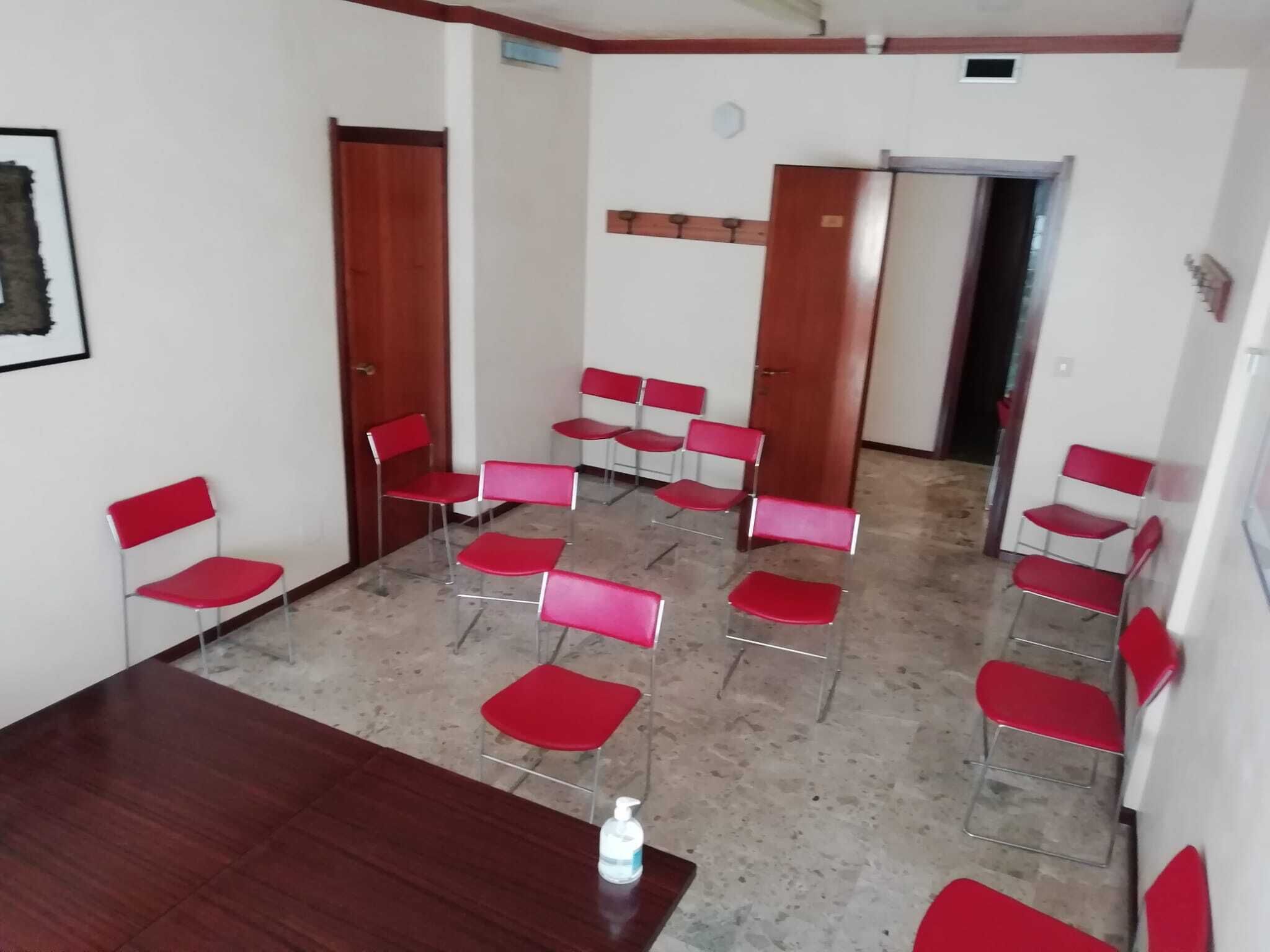 Uma sala de conferências com uma mesa de madeira e cadeiras vermelhas dispostas ao redor.
