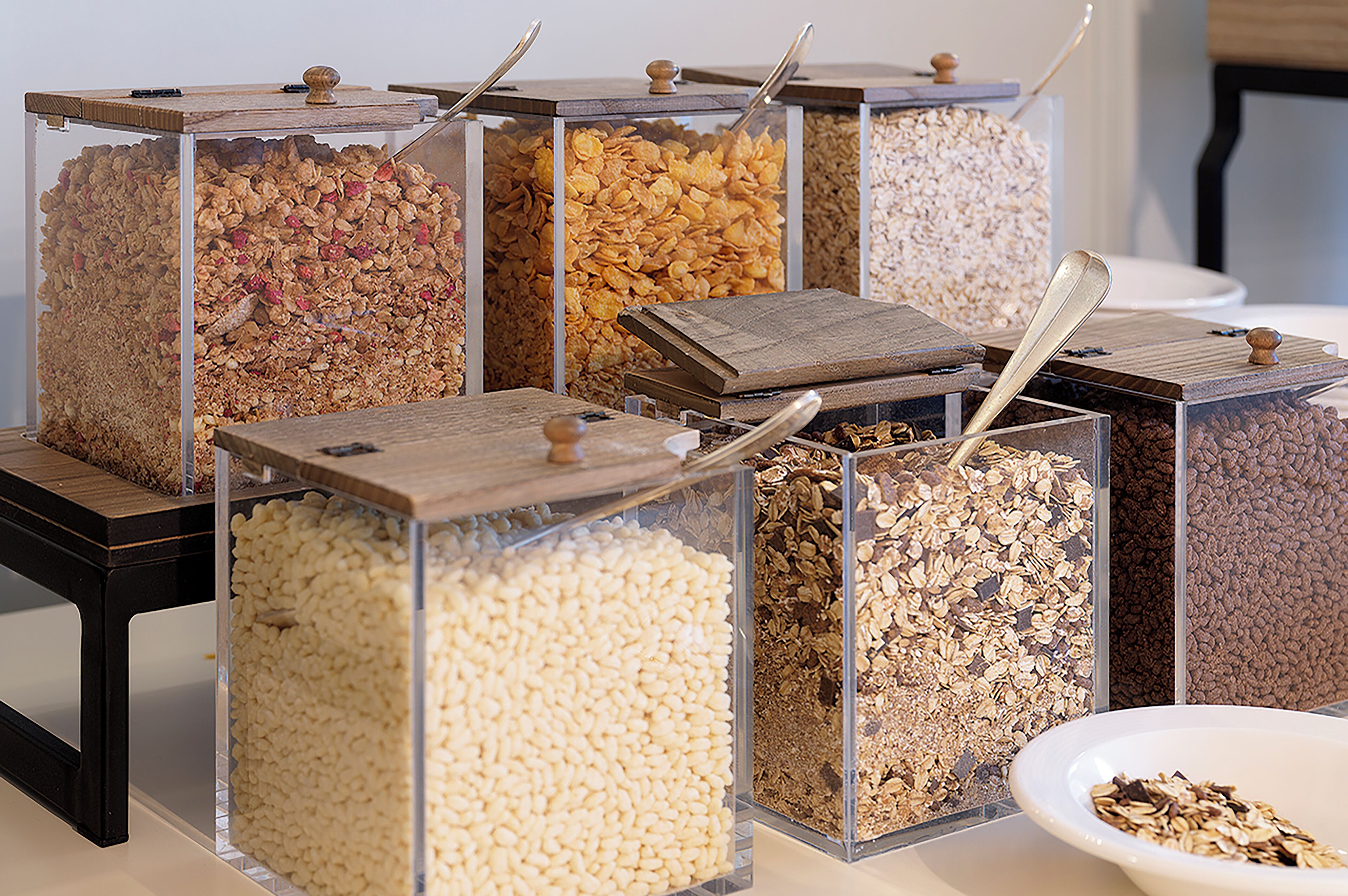 Exposição de várias barras de granola e cereais em recipientes transparentes com tampas de madeira.