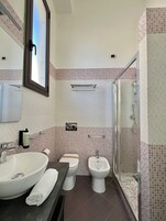 Casa de banho moderna com uma pia grande, duas sanitas, um bidé e cabine de duche envidraçada.