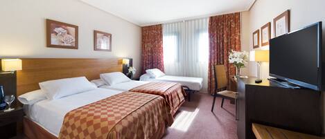 Quarto de hotel com duas camas, uma escrivaninha, uma televisão e uma cadeira.