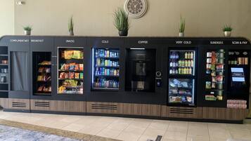 Espaço com máquinas de venda automática, com seções identificadas para lanches, bebidas geladas, café e artigos diversos.