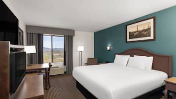 Quarto de hotel com cama, escrivaninha, cadeira, televisão, abajur e quadro na parede.