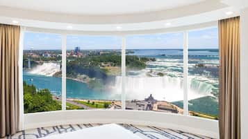 Quarto com uma grande janela panorâmica que oferece vista para uma cascata e um horizonte urbano.