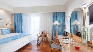 Quarto de hotel com cama, secretária, cadeira, máquina de café e um vaso com flores.