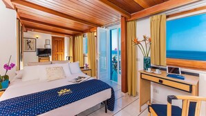 Quarto de hotel com cama, escrivaninha com computador, televisão e vista para o oceano.