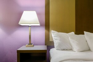 Cama bem arrumada com almofadas brancas e mesa de cabeceira com abajur.