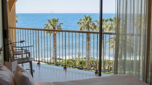 Varanda com vista para o mar, palmeiras e uma cadeira.
