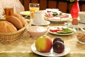 Mesa de café da manhã com pão, frutas, legumes e uma jarra de suco.