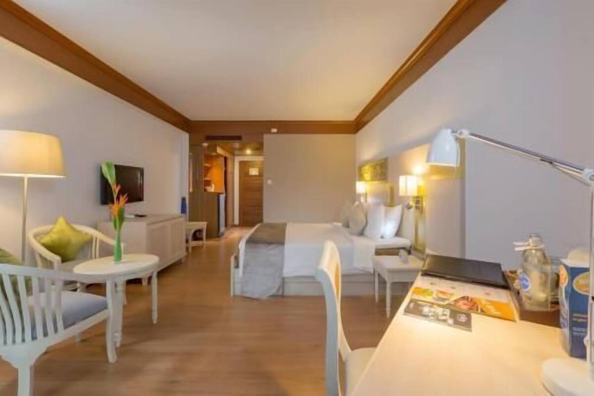 Quarto de hotel com cama, escrivaninha, cadeira, televisão e luminária.