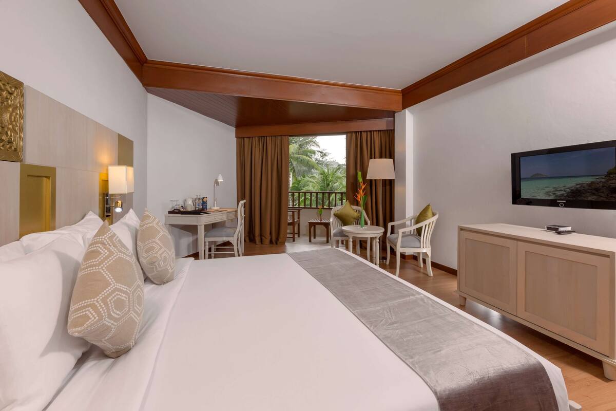 Quarto de hotel com uma cama grande, uma escrivaninha com cadeira, televisão e vista para o exterior.