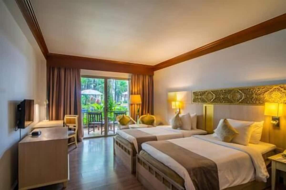 Quarto de hotel com duas camas, uma escrivaninha, uma cadeira e vista para o exterior.