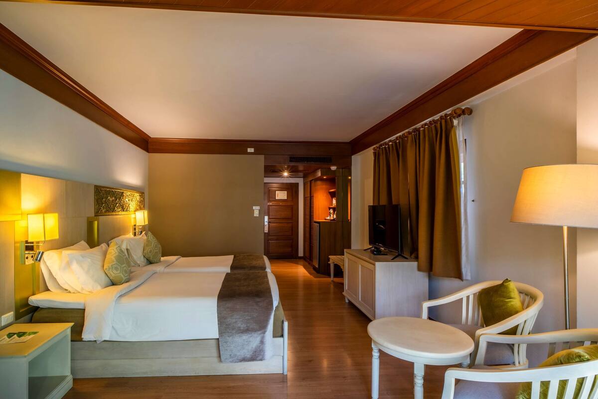 Quarto de hotel com cama, mesa de cabeceira, luminária e uma cadeira.