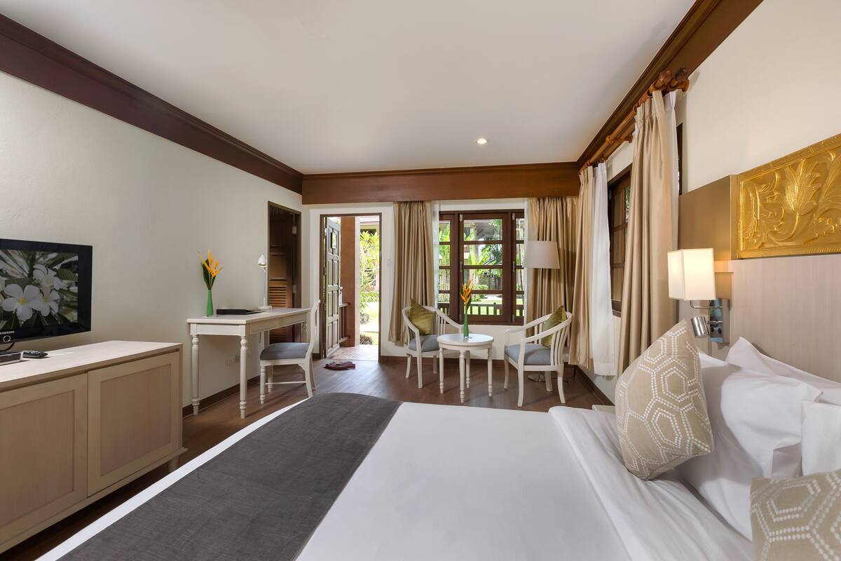Quarto de hotel com cama, escrivaninha, cadeiras e televisão.
