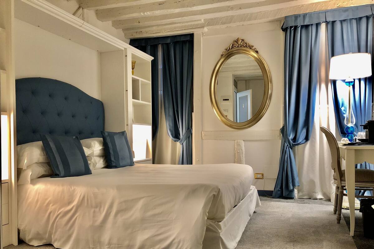 Quarto de hotel com uma cama grande, uma escrivaninha, uma cadeira, um guarda-roupa e um espelho.