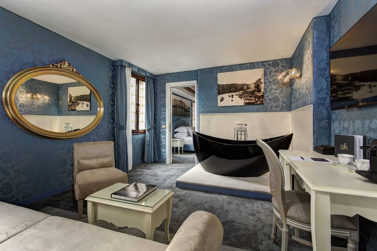 Quarto com um espelho grande, banheira, mesa de jantar e sofá.