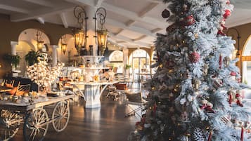 Um amplo hall de hotel com uma grande árvore de Natal, uma carruagem antiga e lustres elegantes.