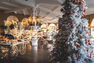 Um amplo hall de hotel com uma grande árvore de Natal, uma carruagem antiga e lustres elegantes.