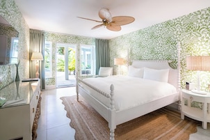 Quarto com cama, cortinas, ventoinha no teto, mesa de cabeceira e televisão.