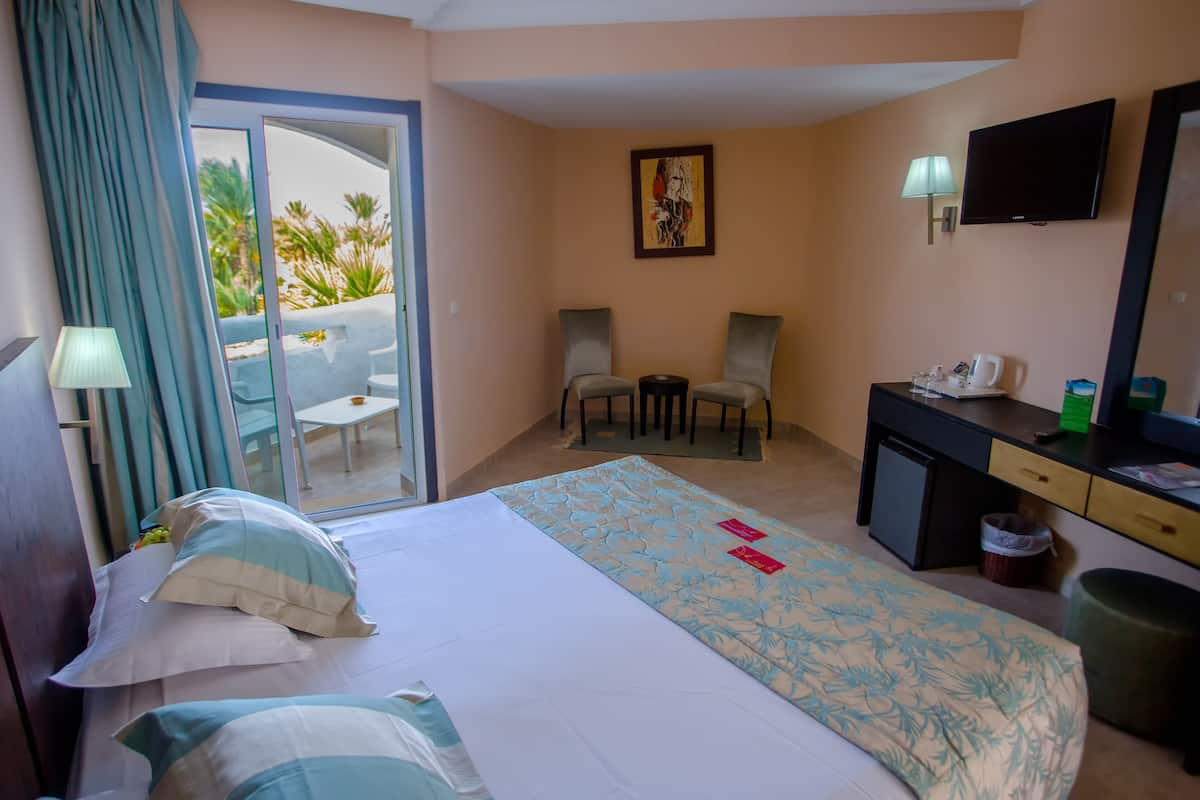 Quarto de hotel com cama, escrivaninha, poltrona, televisão e vista para o exterior.