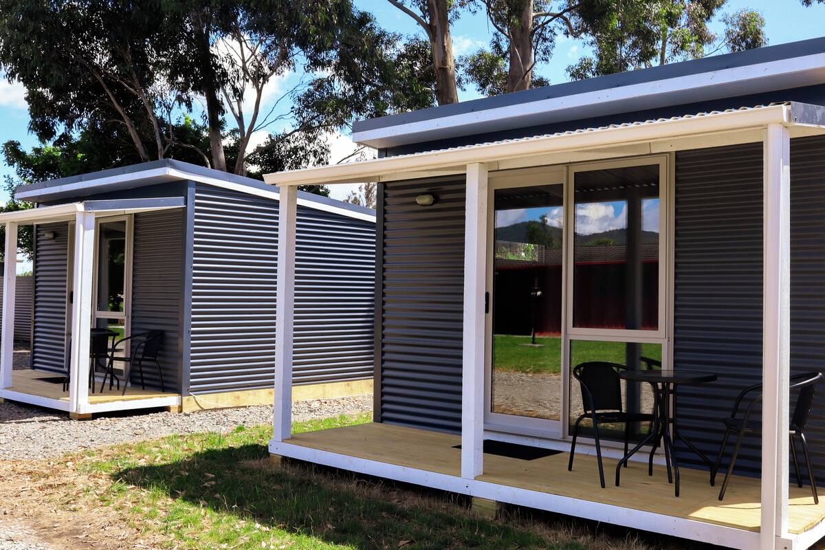 Duas casas móveis modernas e compactas, com portas deslizantes, cada uma com um pequeno alpendre com mesa e cadeiras.