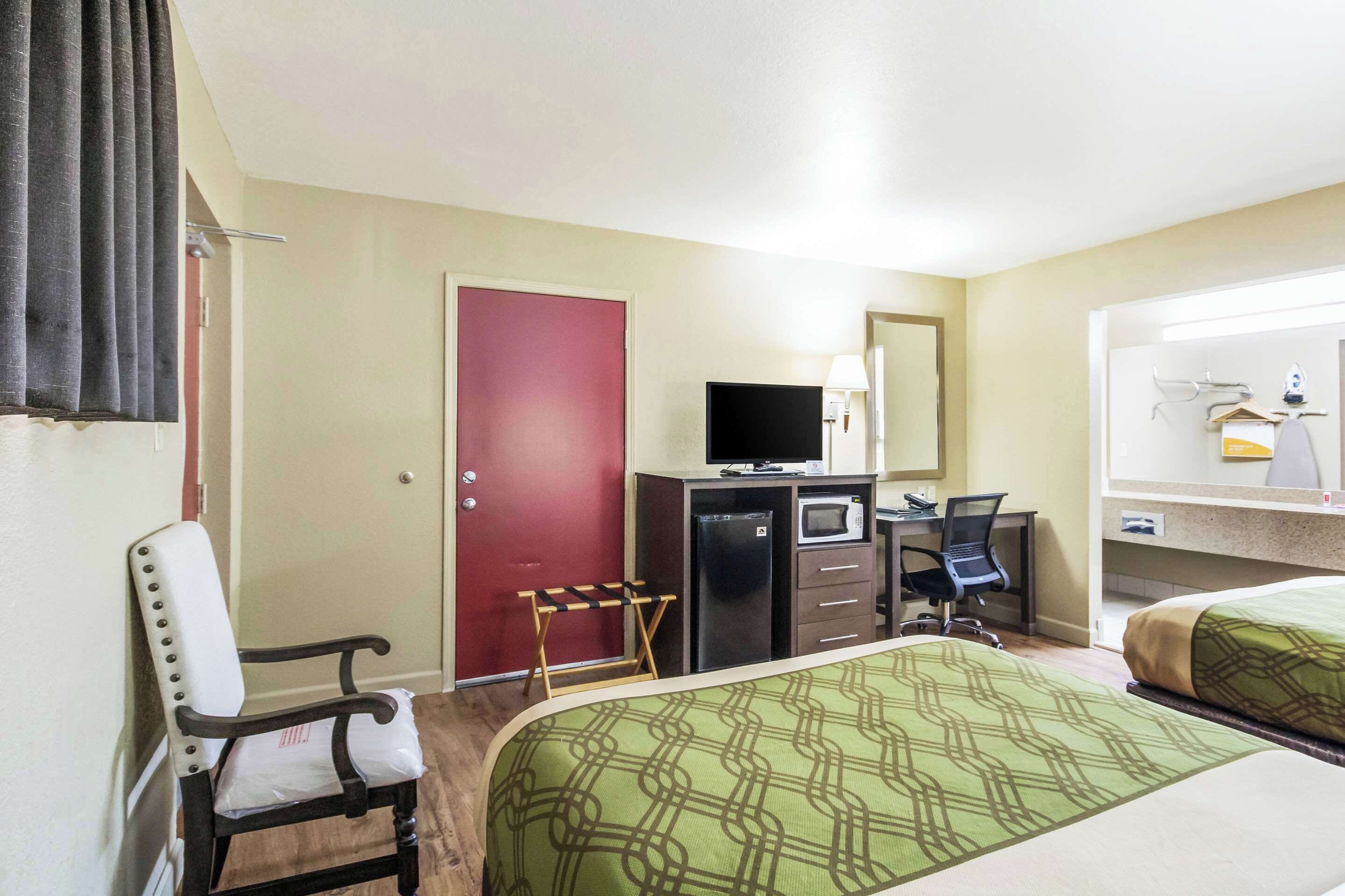 Quarto de hotel com duas camas, uma mesa de trabalho, televisão, uma cadeira, guarda-roupa e porta.